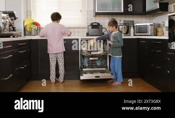Two kids collaboratively load dirty dishes into an open dishwasher in a ...