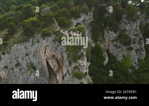 Tourist waves at a drone camera while standing on top of cliff on an ...