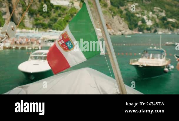 Italian flag fluttering on a boat with a blurred backdrop of the Amalfi ...