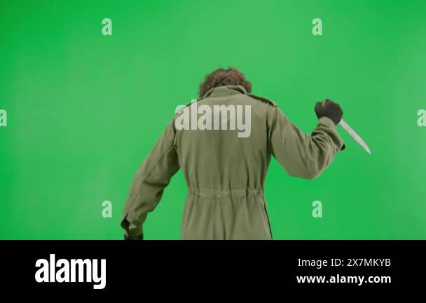 A maniac in green overalls with a knife in his hand walks and looks ...