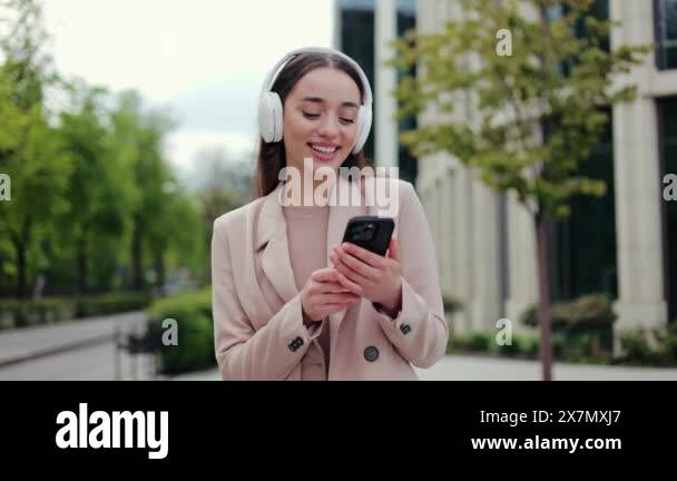 Ecstatic woman in classic wear listening music and walking on sidewalk ...
