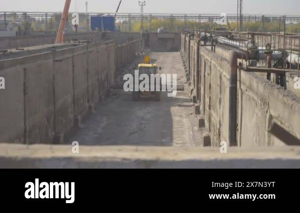 Excavator carries concrete beam passing in empty basin of primary ...