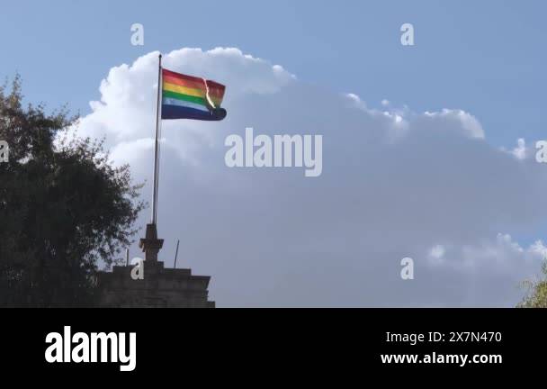 A rainbow flag is flying high in the sky. The flag is on a pole and is ...