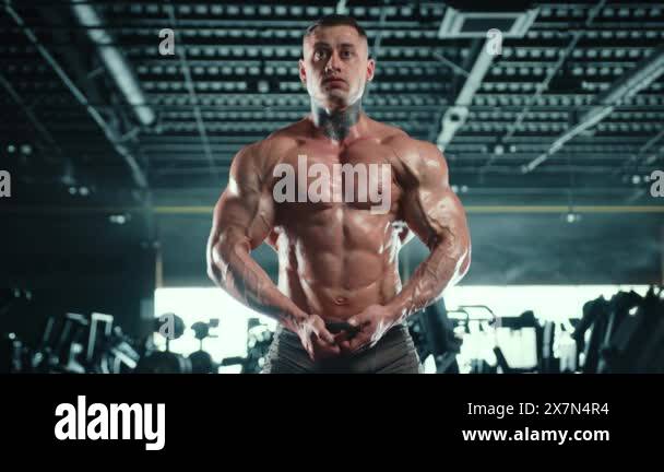 A well-built bodybuilder poses powerfully in the gym, his rippling ...