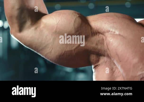 The camera zooms in on a mans flexed bicep as he performs a bicep curl ...
