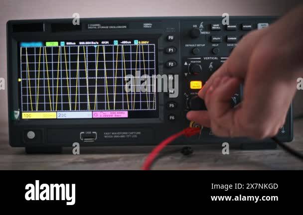 A hand adjusts the settings on a modern oscilloscope, changing the display of a sine wave. Close ...