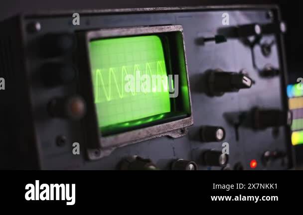A vintage oscilloscope displays a moving sinusoidal waveform on its ...