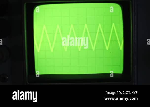 Close-up of a vintage oscilloscopes CRT screen where a green waveform ...