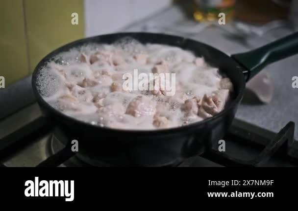 Raw chicken meat is being cooked in a frying pan on the stove. Bubbles ...