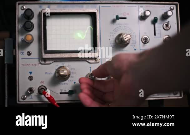 Zoom in on a hand adjusting knobs on a vintage oscilloscope ...