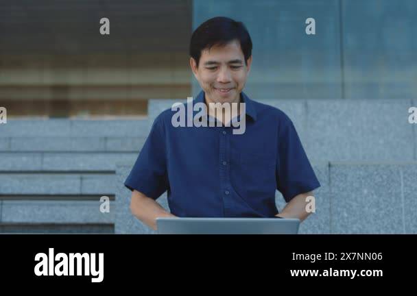 Happy Asian Gentleman Sitting Outdoors, Engaged in Laptop Work, and ...