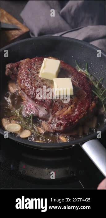 Chef pours melted butter on a juicy beef steak frying on a pan in the ...