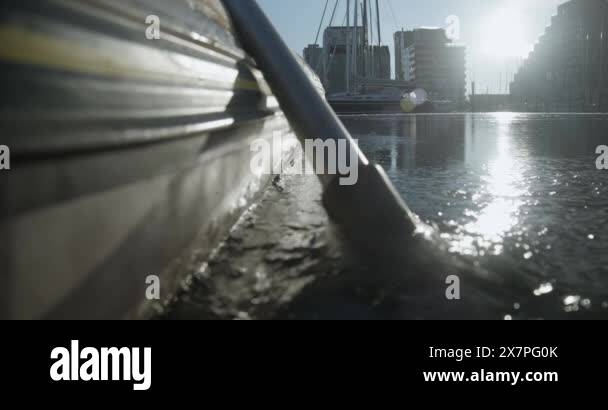 A close-up view of the side of a boat shows an oar partially submerged ...