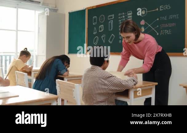 Smart teacher checking cute student homework while explaining idea at class. Attractive ...