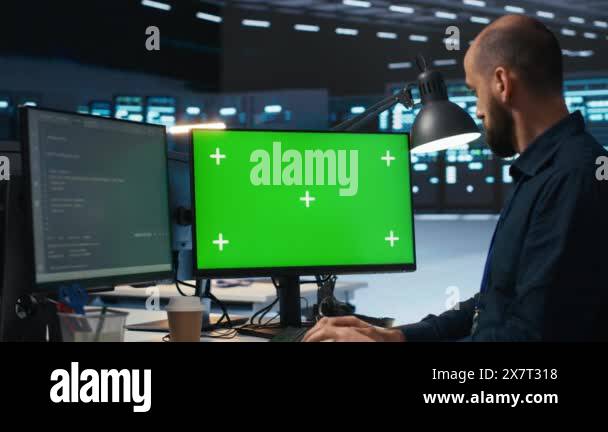 System administrator working on green screen computers in data center, ensuring optimal ...