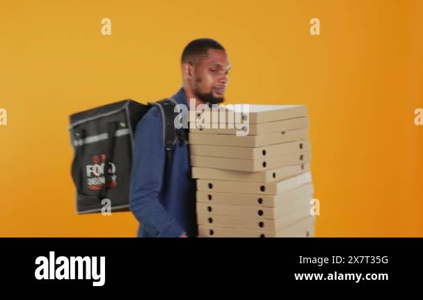 Male pizzeria courier carrying huge pile of pizza boxes in studio ...