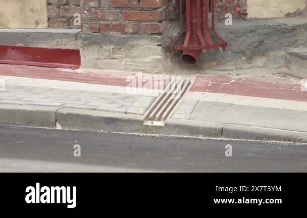 Red downspout connected to a brick building, with a drainage channel on ...