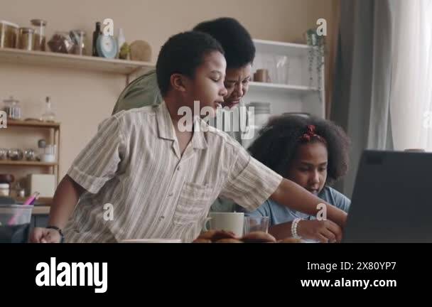 Medium of school-aged African American boy and girl doing homework with help of caring short ...