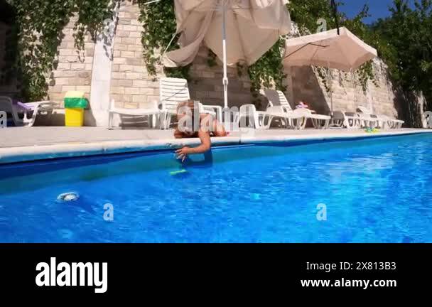 Little girl is trying to get a bottle of soap bubbles from the pool by ...