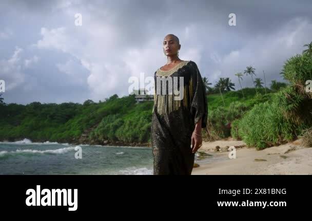LGBTQIA black person in glittering dress walks on stunning sea shore ...