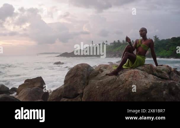 Divine non-binary black person in long open dress, brass jewelry poses ...