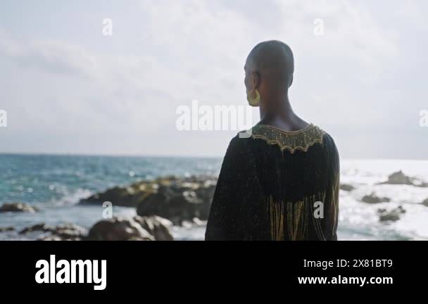 LGBTQIA black person in shimmering dress looks at stunning stormy ocean ...