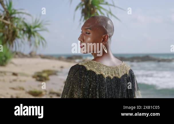 LGBTQIA black person in luxury dress walks, turns back on stunning sea ...