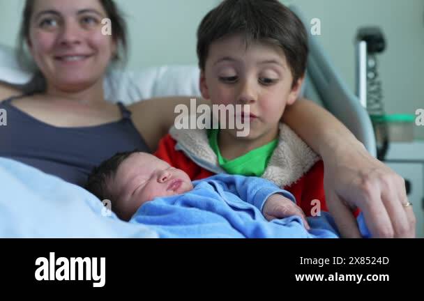 Mother watches lovingly as older sibling cradles newborn baby ...