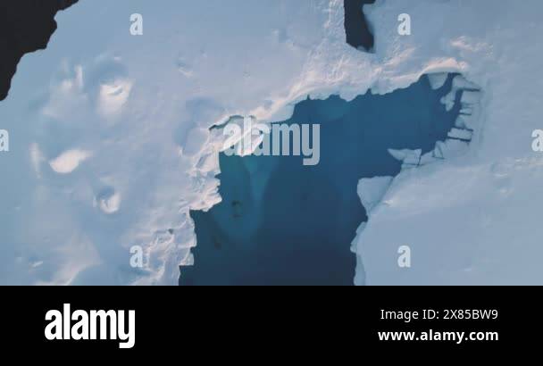 Melting cave in ice floe snow covered iceberg aerial top down view ...