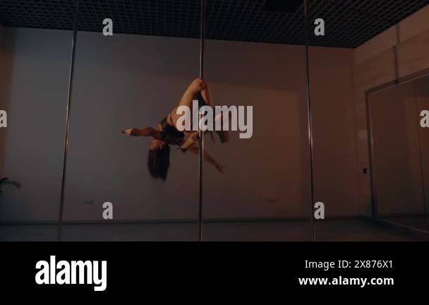 Woman in leather underwear gracefully pole dancing in a dimly lit room ...