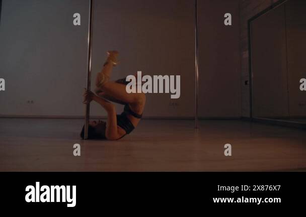 Woman in leather underwear gracefully pole dancing in a dimly lit room. Slow motion. Elegant ...