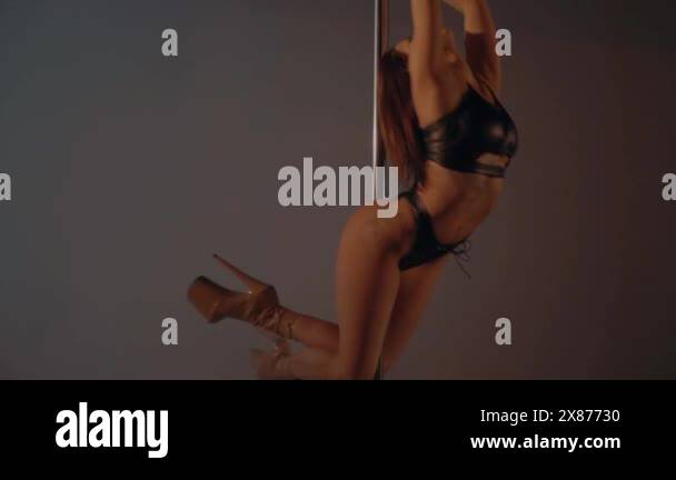Woman in leather underwear gracefully pole dancing in a dimly lit room. Slow motion. Elegant ...