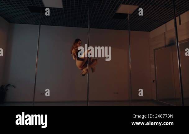 Woman in leather underwear gracefully pole dancing in a dimly lit room. Slow motion. Elegant ...