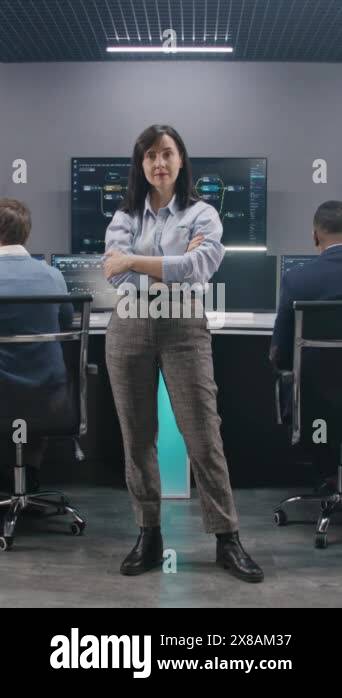 Female big data scientist stands in monitoring room and looks at camera ...