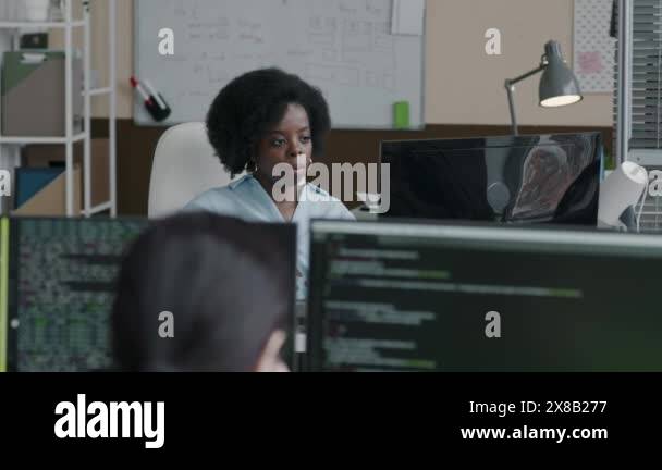 Young Black woman using desktop computer while working in minimalist style office with female ...