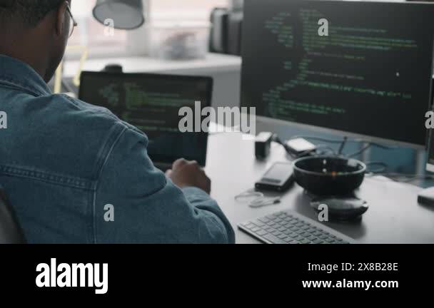 Back view slowmo of Black male system administrator sitting in front of ...