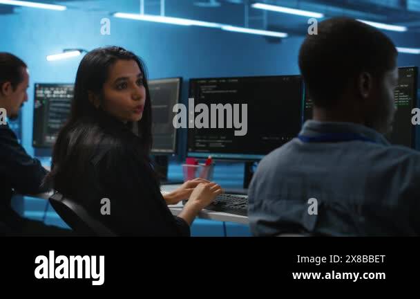 Multiethnic team of engineers working in high tech server hub, using PCs to analyze data ...