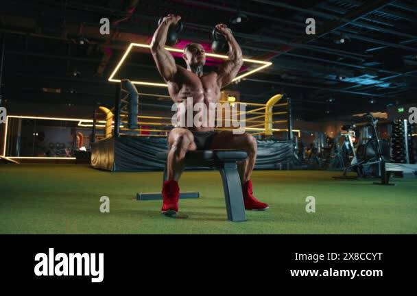 Muscular bodybuilder performing a seated dumbbell shoulder press in a ...