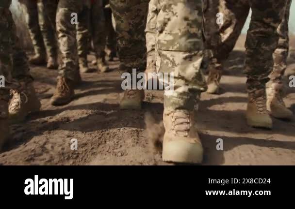 A close-up reveals the dusty boots of soldiers marching in unison through sandy terrain ...