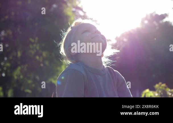 Little girl smiles widely at sun rays and raises arms up, radiating ...