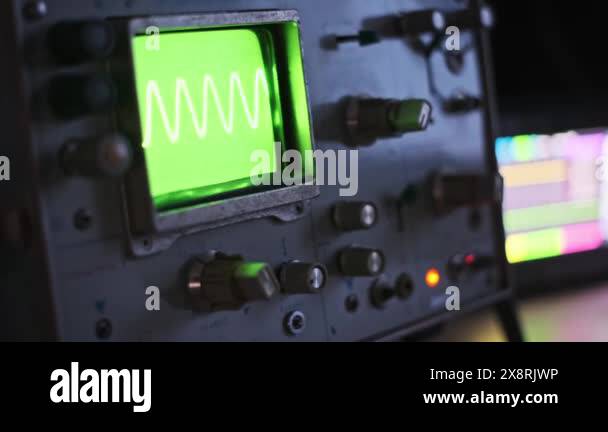 Close-up of a vintage oscilloscope, its green CRT screen displaying fluctuating waveforms ...