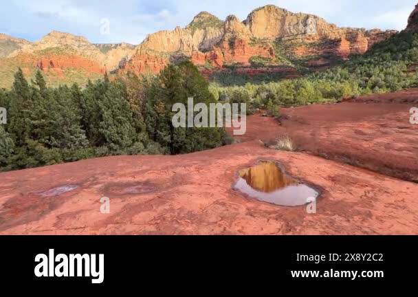 A red rock plateau with small water puddles reflecting the surrounding ...