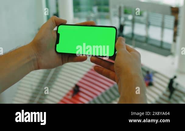 Close-up of male hands holding a smartphone with a green screen display ...