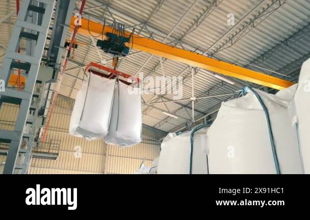 An industrial crane lifts large white bags in a spacious warehouse The ...
