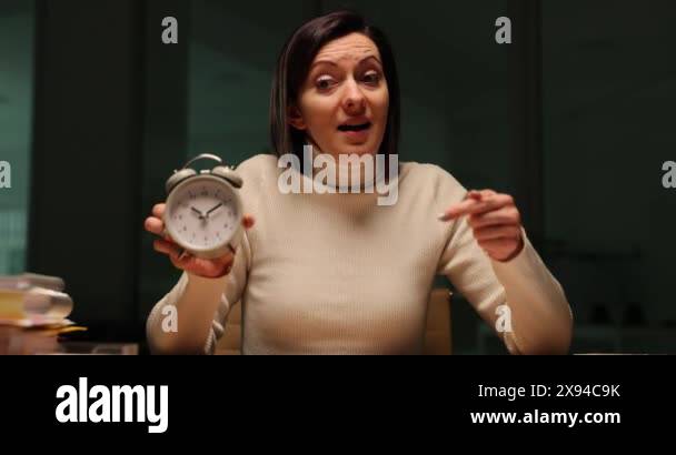 Woman manager points to alarm clock late at night in office. Time is ...