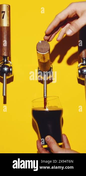 Bartender slowly pouring delicious dark beer in glass against yellow ...