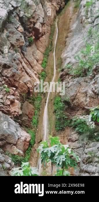 A small waterfall falls between rocks from a great height. The small ...