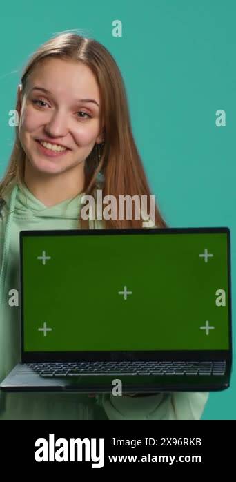Vertical video Smiling woman presenting laptop with green screen ...
