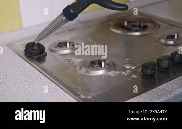 Close-up steam cleaner being used to deep clean a greasy gas stove. The ...
