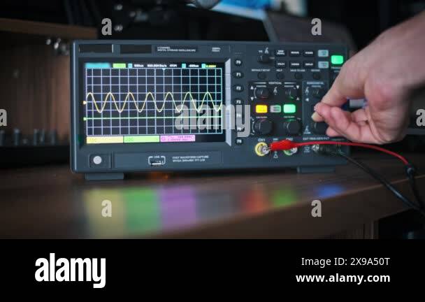 A persons hand is shown adjusting the knobs on a modern oscilloscope to ...